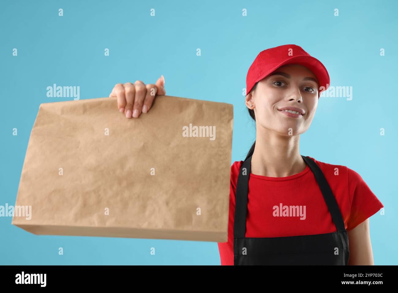Fast-food worker with paper bag on light blue background Stock Photo ...