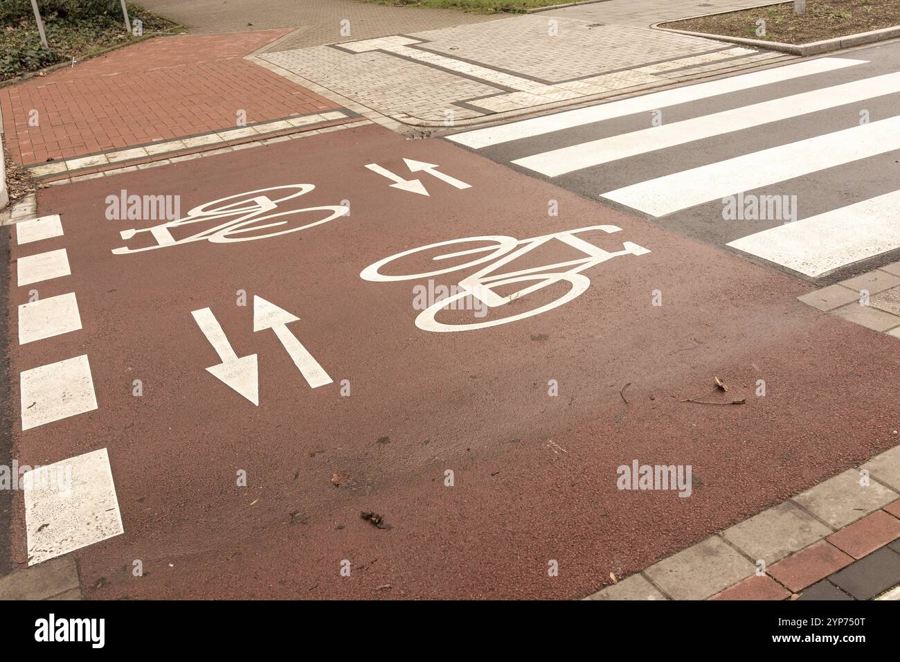 A city street featuring a bicycle lane and crosswalk with red pavement ...