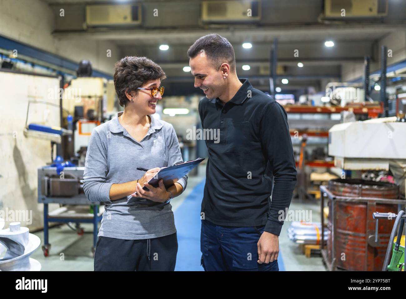 Male worker talking happily to a female workshop manager while writing on clipboard Stock Photo ...