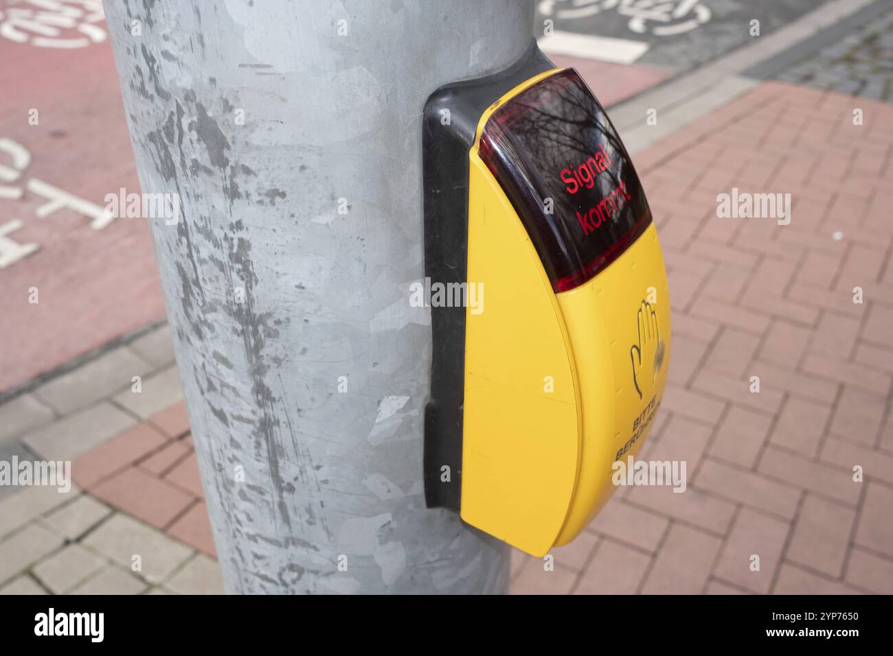 Yellow pedestrian crossing button mounted on a pole in an urban area ...