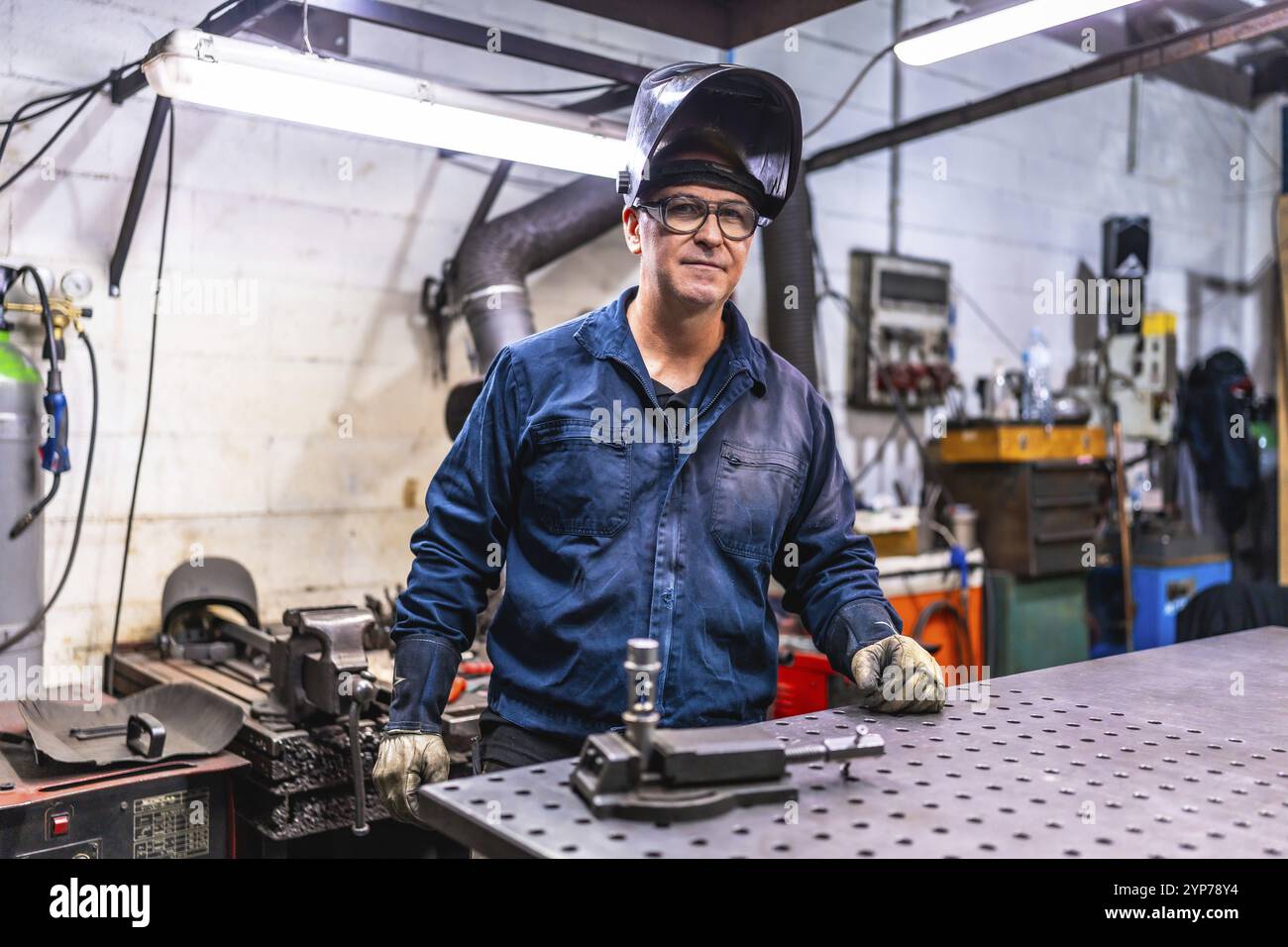 Mature male welder in a metal factory taking a break standing looking ...