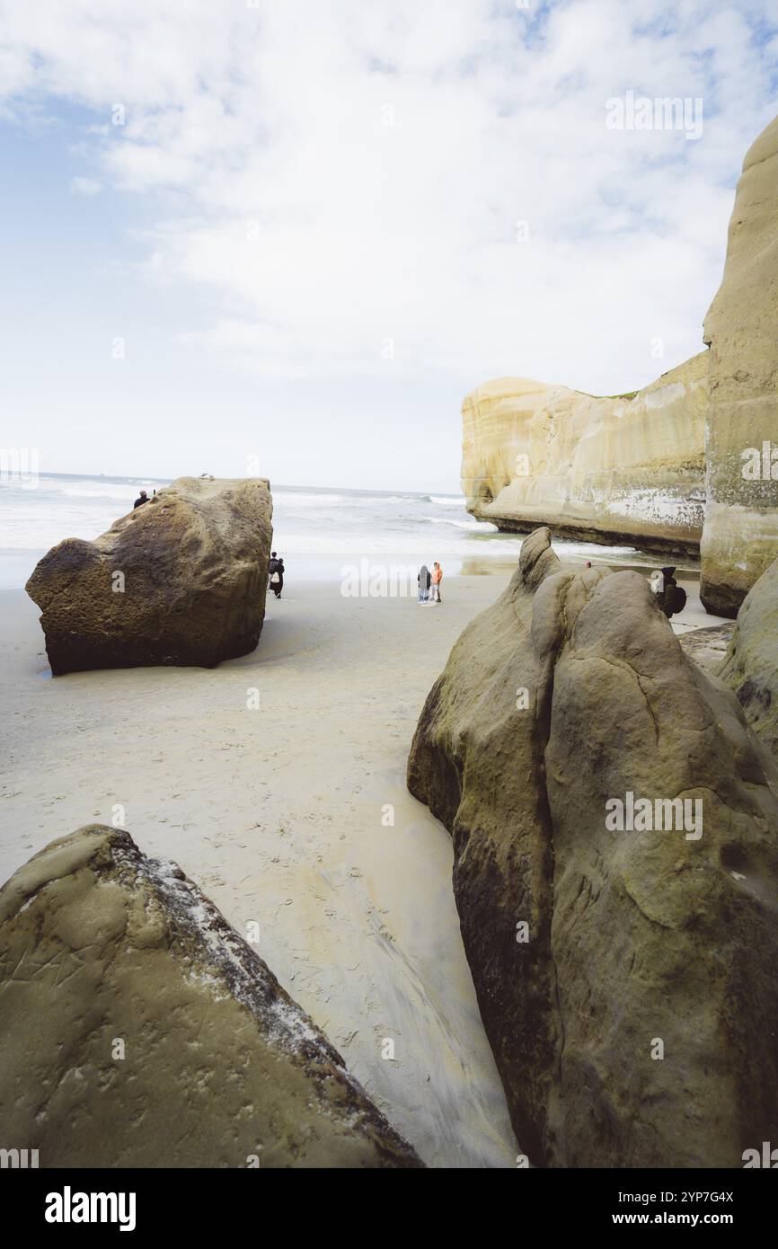People walking on a wide, rock-lined beach, Dunedin, New Zealand ...