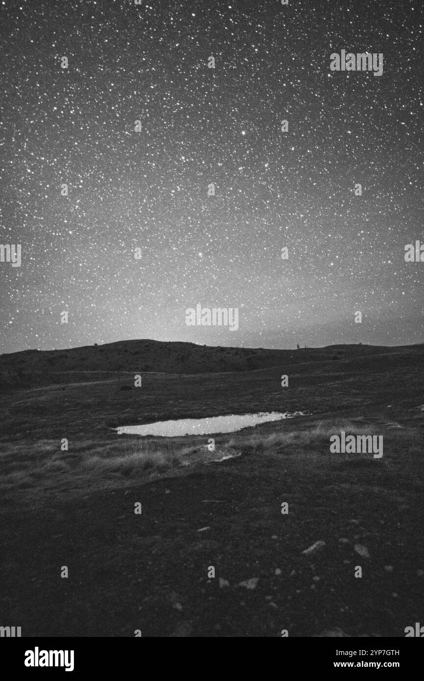 Night scene with starry sky and reflecting puddle on hilly terrain in ...