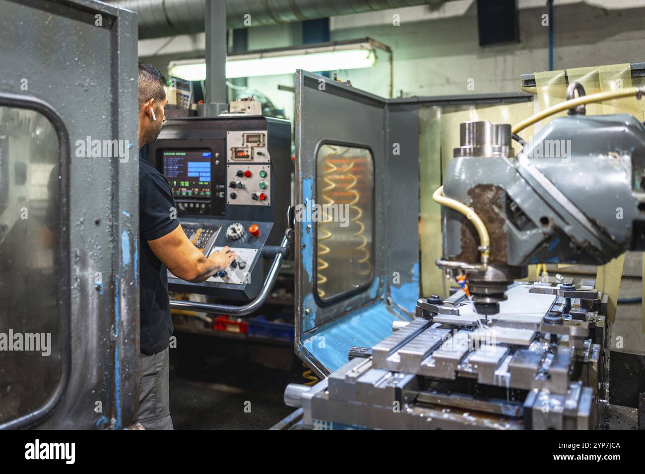 Rear view of a male worker using panel station of milling machine in a ...