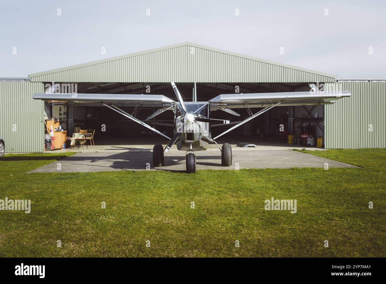 A small single-engine aircraft stands in front of an open hangar on a ...