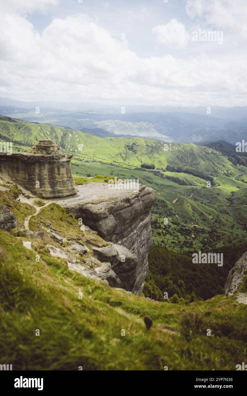 A dramatic rocky outcrop overlooks green hills and a mountainous ...