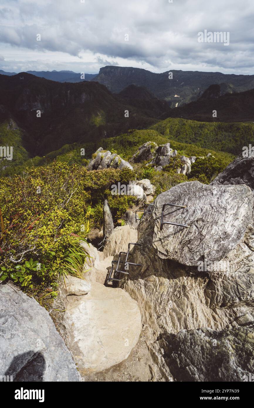 Rough rocks and a small path with views of forested mountains ...