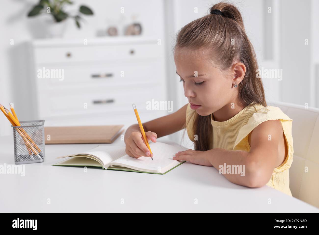 Girl with correct posture doing homework at white desk indoors Stock ...