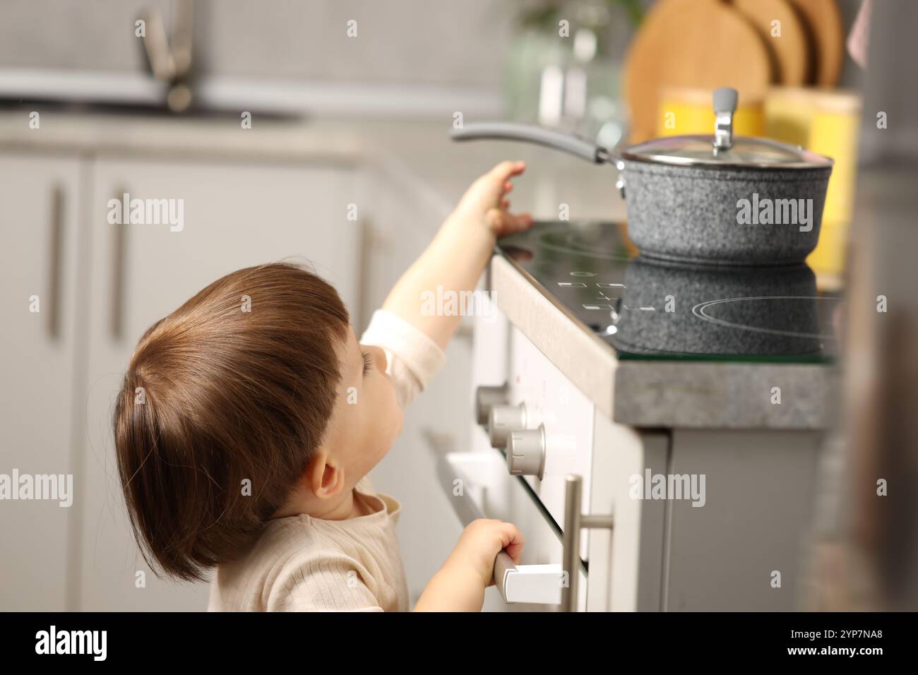 Little boy playing with pot on stove in kitchen. Dangerous situation ...