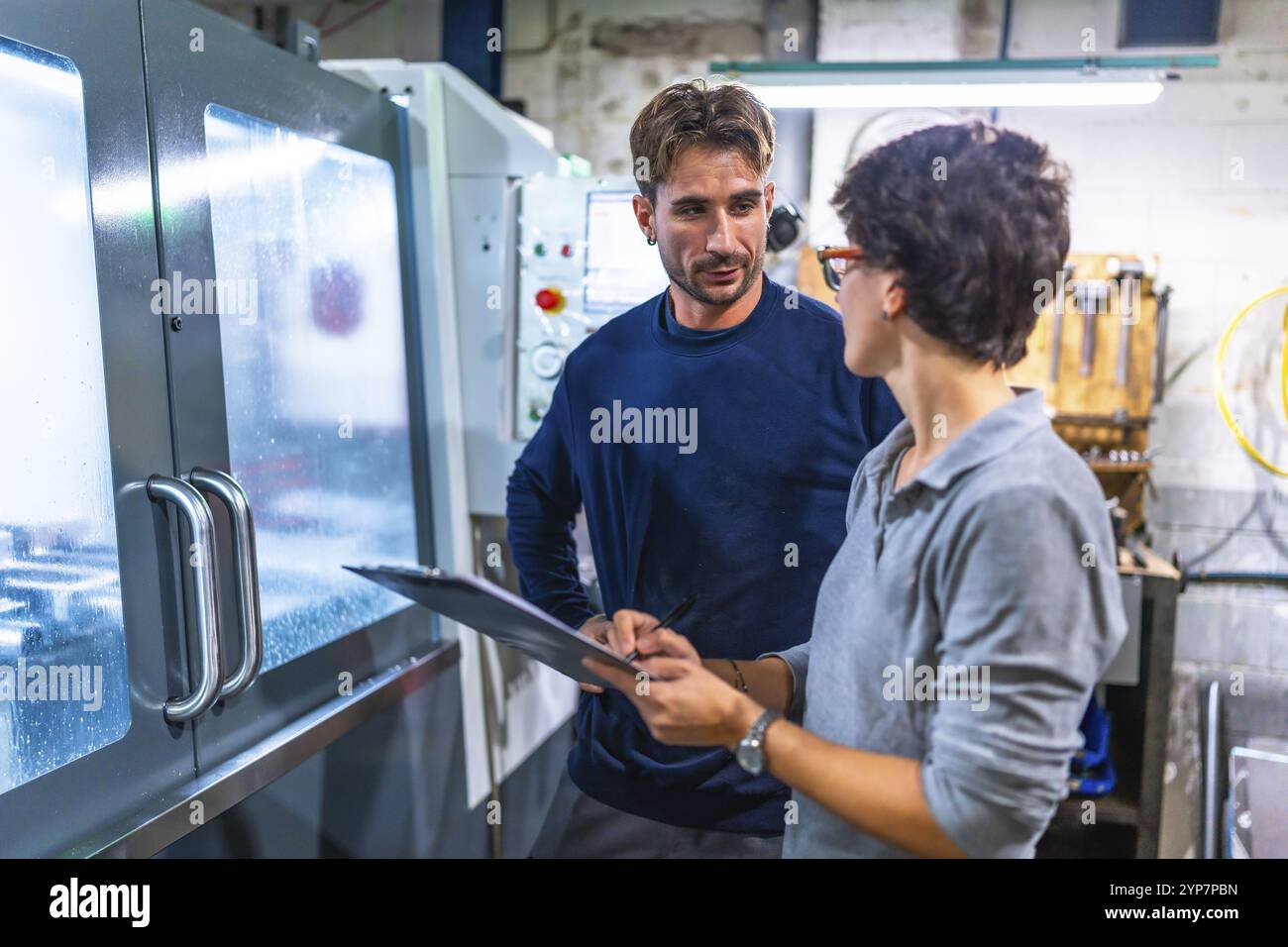 Female manager writing notes in a clipboard and manual worker talking ...