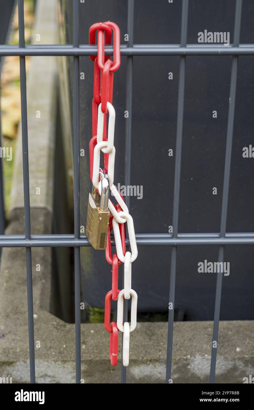 Red and white plastic chain and metal padlock securing a metal fence ...