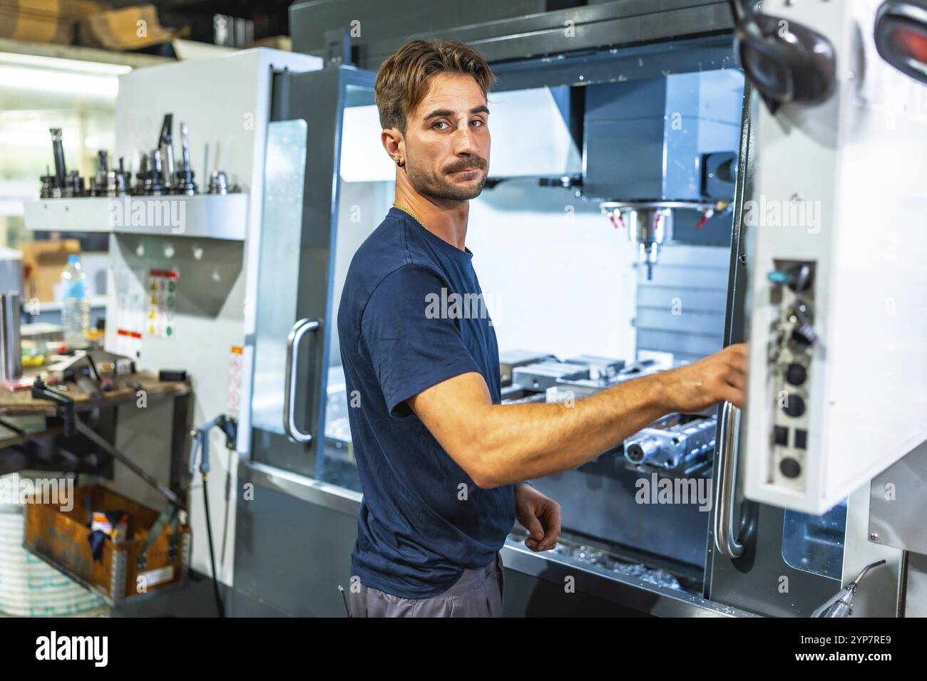 Man turning to look at camera while using mechanical machine to shape ...