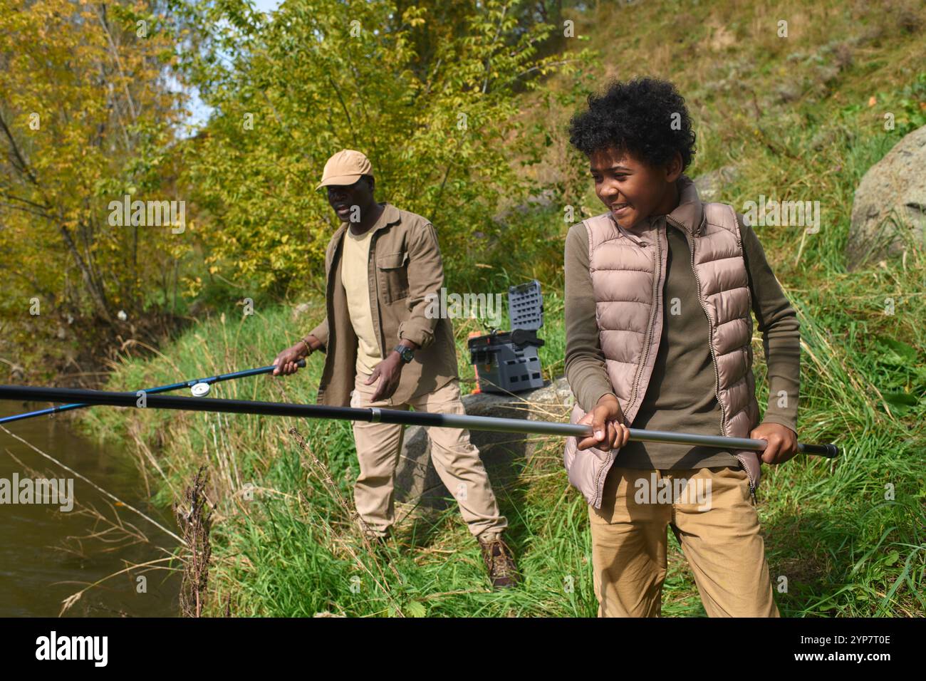 Medium close up of excited boy with huge fishing rod in his small hands ...