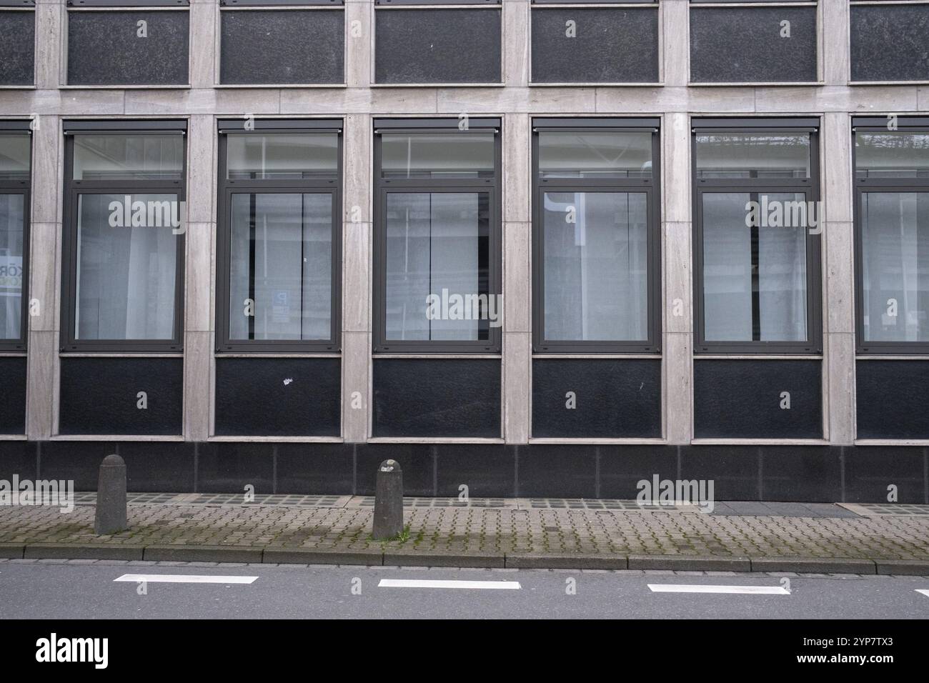A modern building facade with multiple windows and a stone sidewalk ...