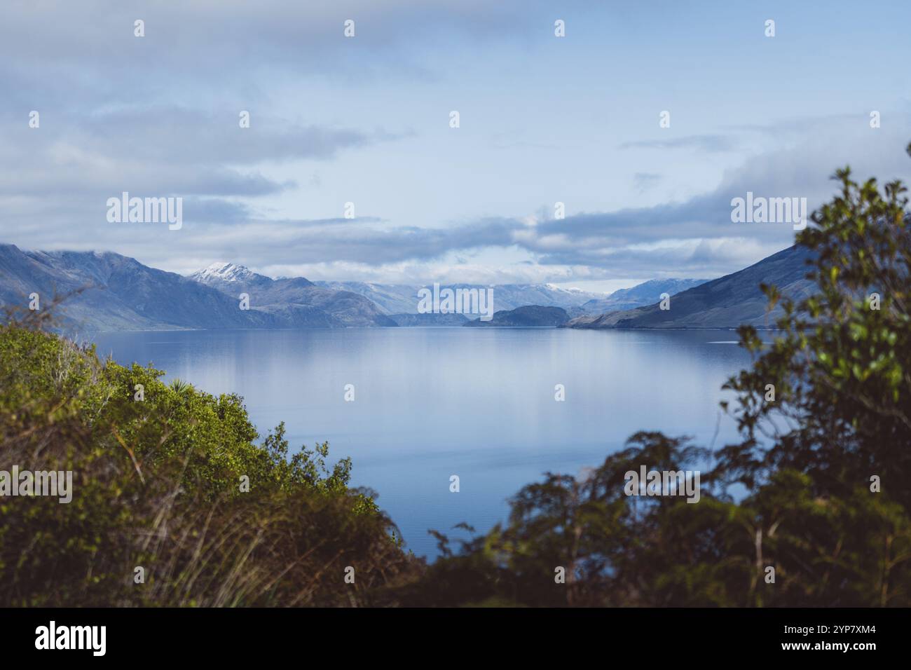 Expansive lake surrounded by mountains and vegetation under a blue sky ...