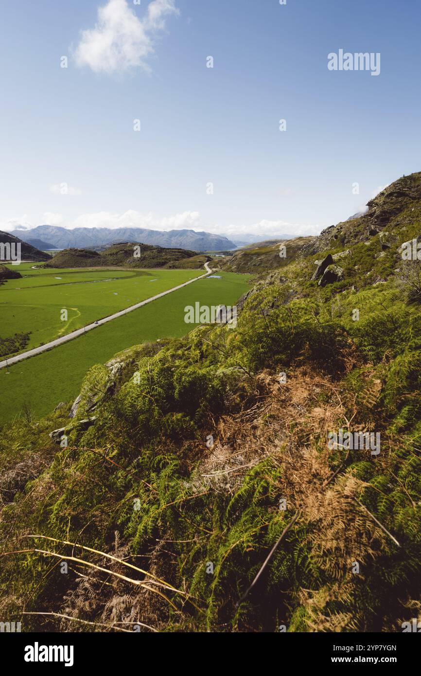 A narrow dirt track winds through green meadows surrounded by hills ...