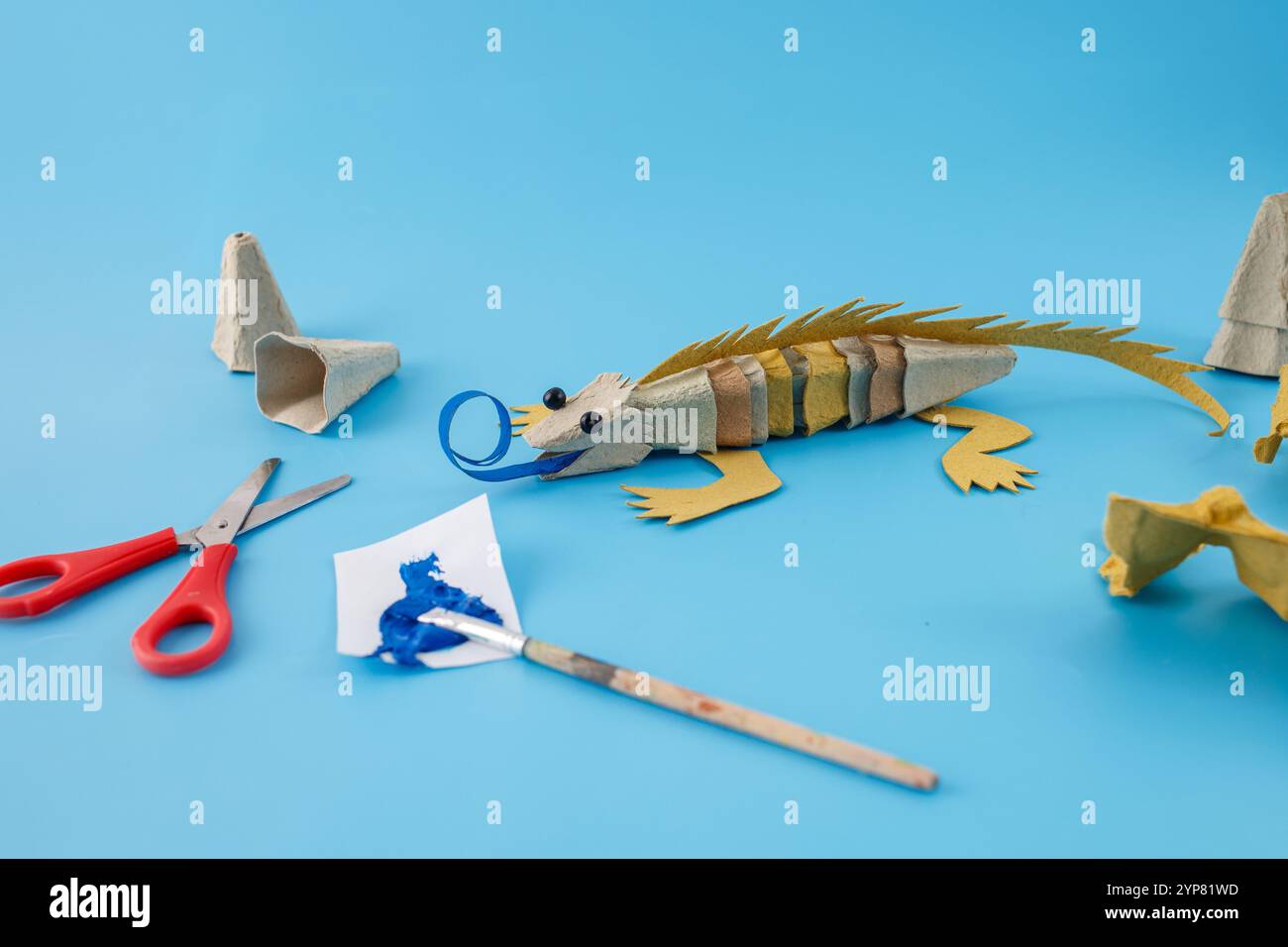 Recycled cardboard iguana craft with scissors, paintbrush, and blue ...