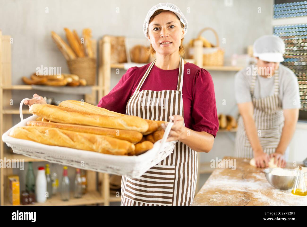 Positive woman baker in uniform baking fresh baguettes in bakery Stock ...