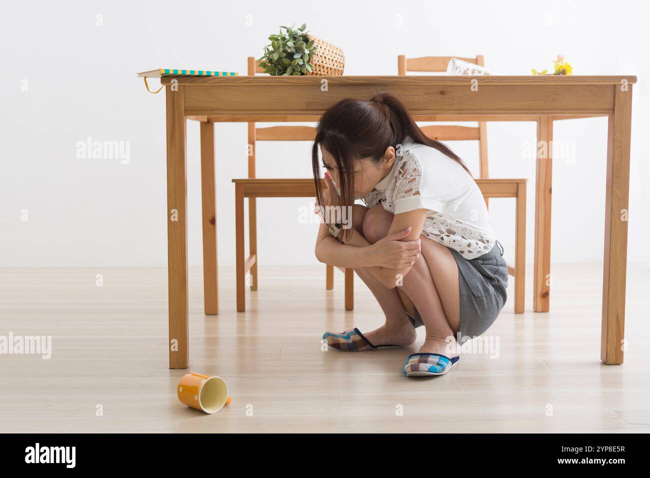 Woman taking shelter under a table from an earthquake Stock Photo - Alamy