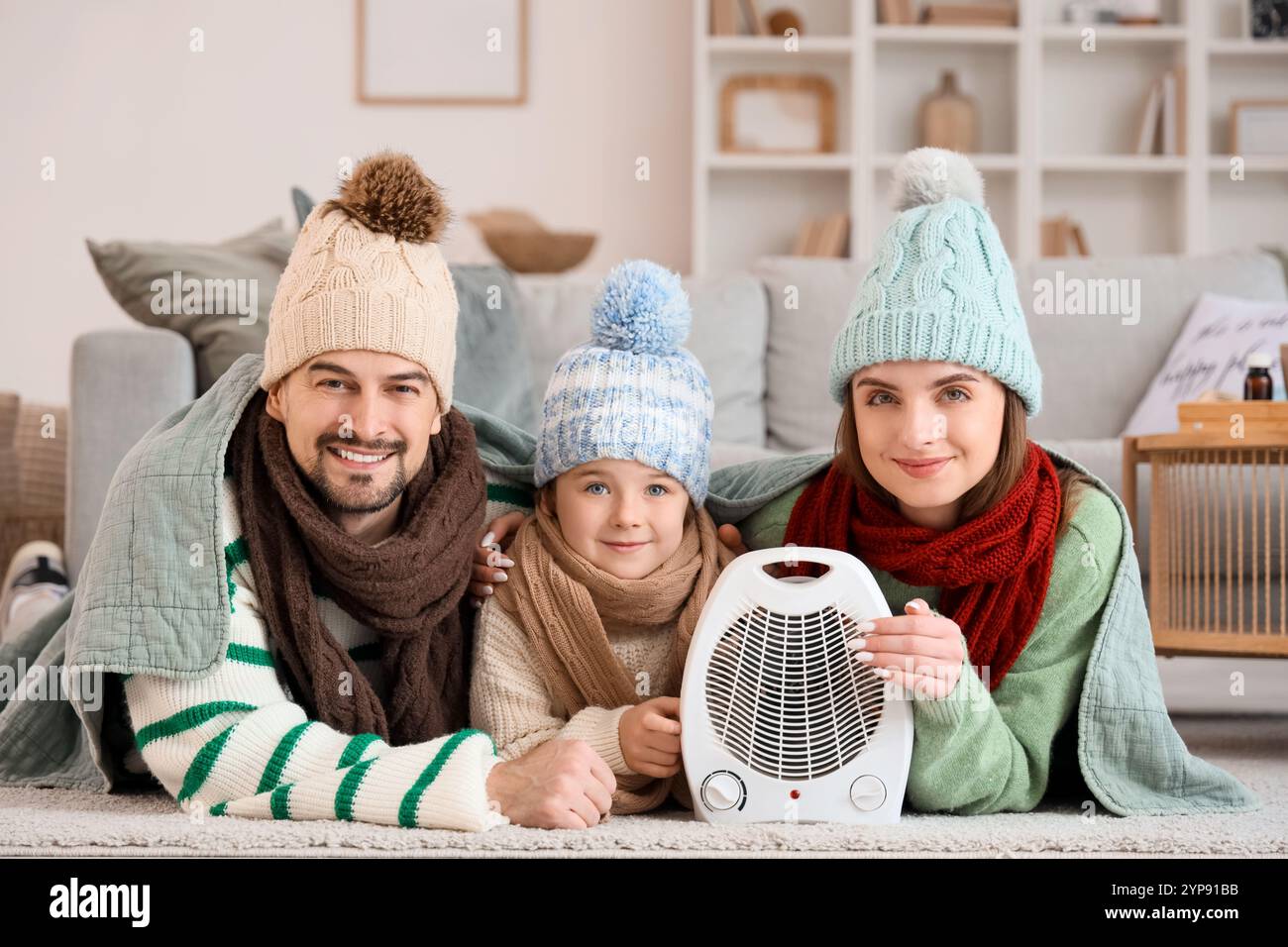 Frozen family with electric fan heater lying on floor at home Stock ...