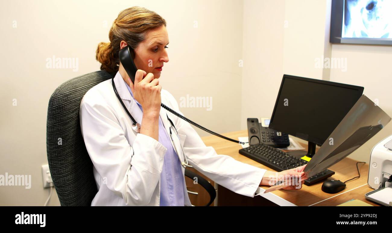 Female doctor examining an x-ray while talking on telephone at the ...