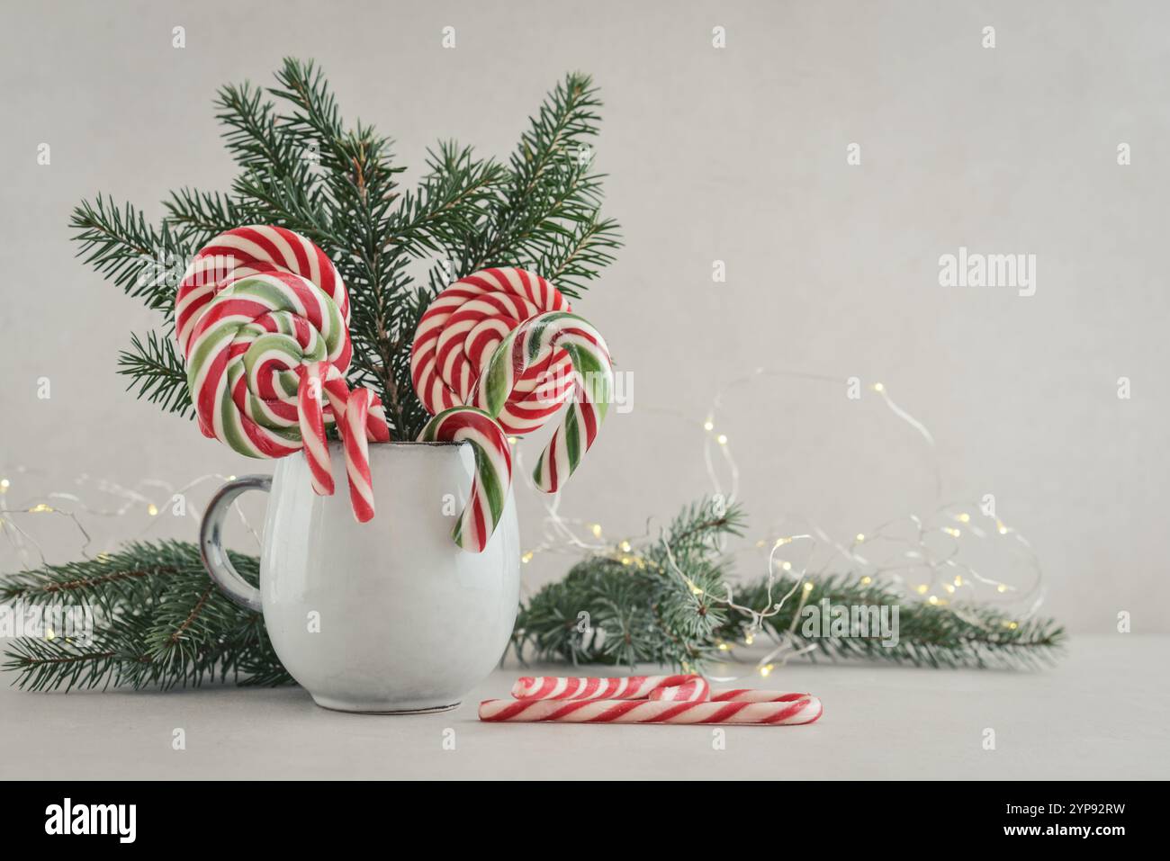 Christmas candy canes, lollipops and fir tree twigs in a mug on light ...