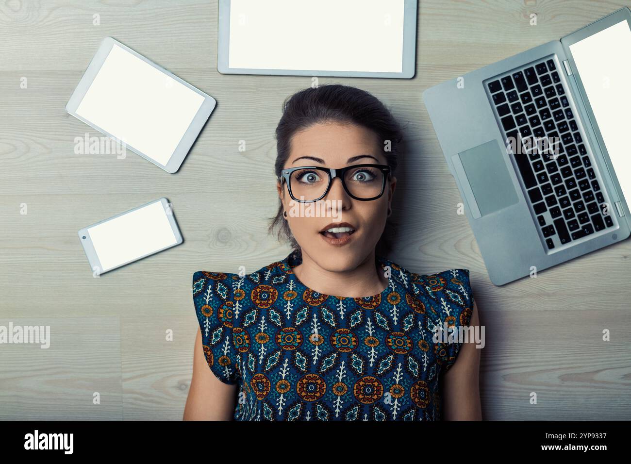 Young adult woman lying on the floor with several electronic devices ...
