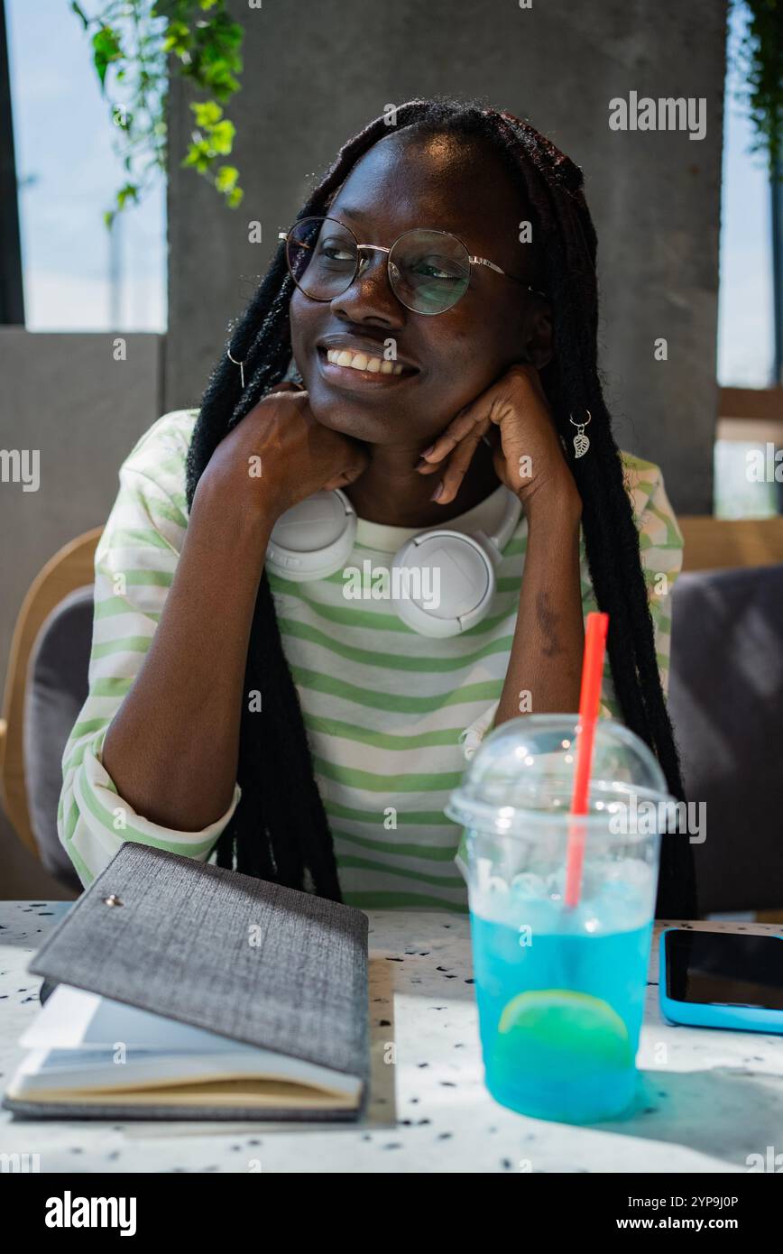 Young black female student smiles happily at a cafe table with a blue ...