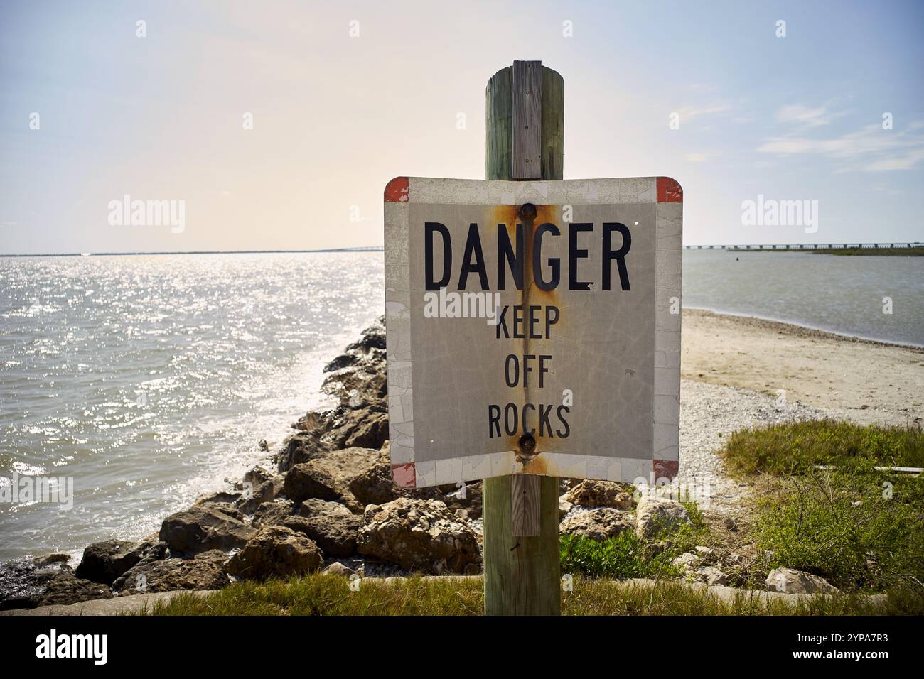 A warning sign stands on the edge of a rocky shoreline Stock Photo - Alamy
