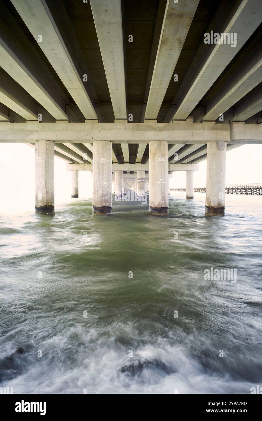The view from beneath a sturdy concrete pier reveals calm water flowing ...