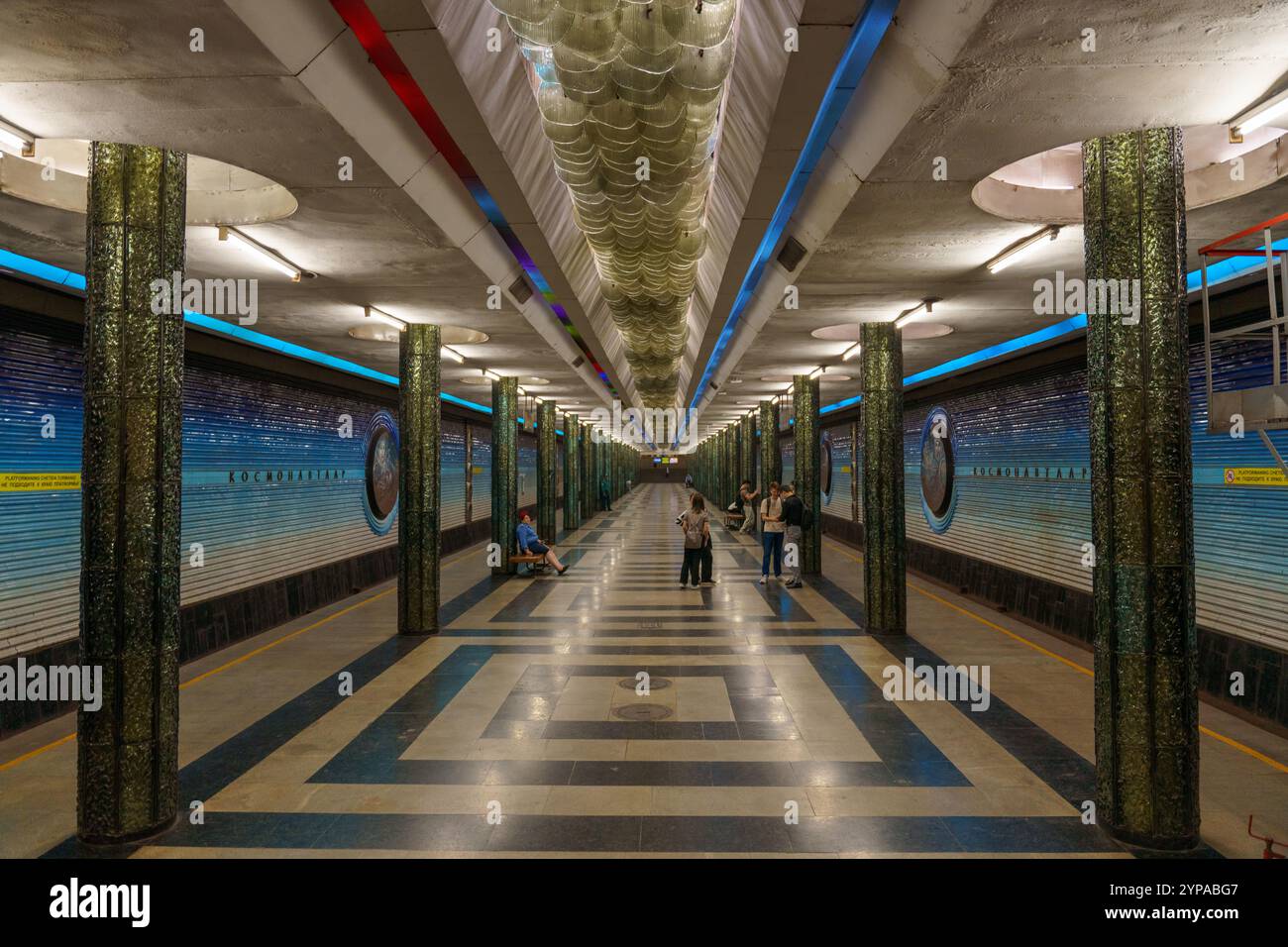 A long, empty subway train station with a blue and white tile floor ...