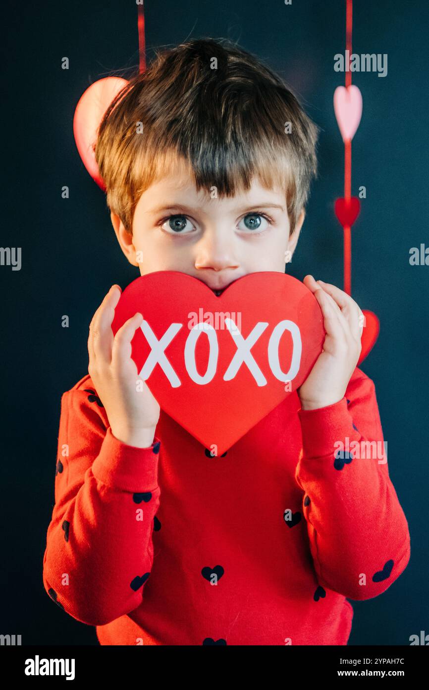 Boy in red pajamas holding a red "XOXO" heart with a sweet gaze Stock ...