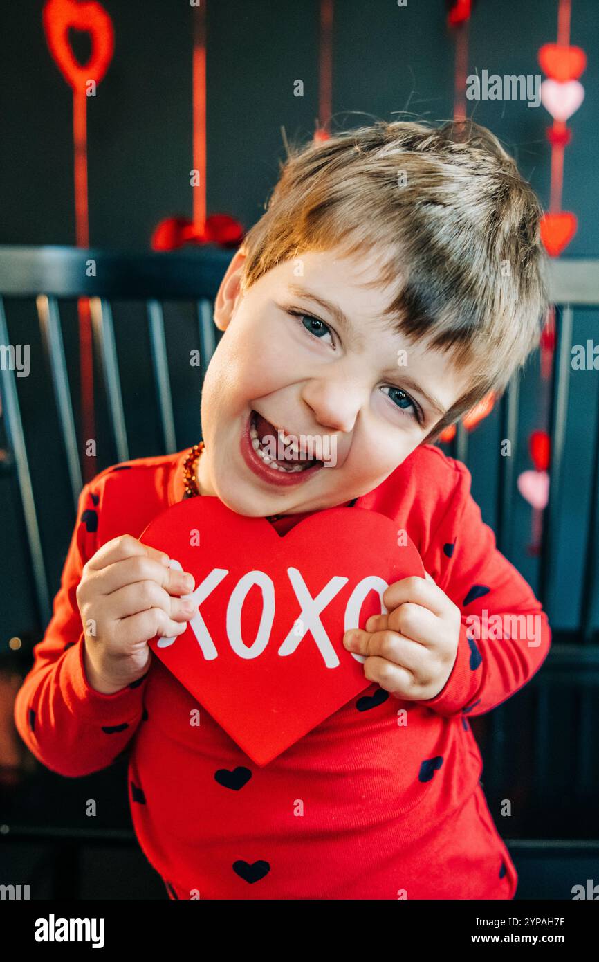 Laughing boy holding a red "XOXO" heart with a playful pose Stock Photo ...