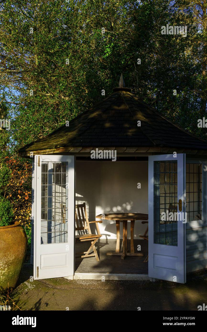 A charming white wooden garden summerhouse with sunlit chairs and a ...