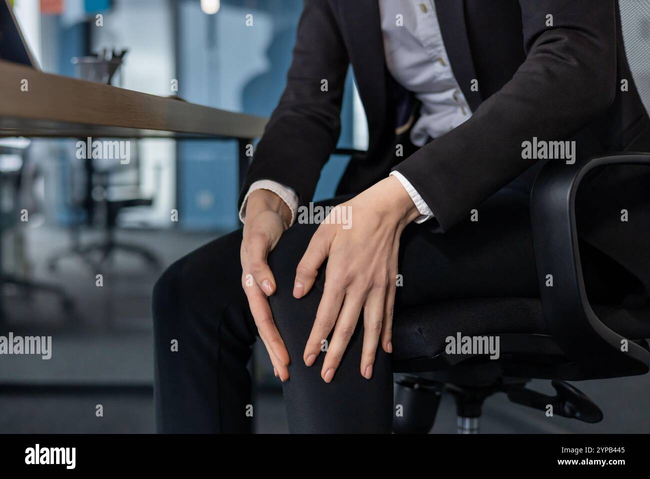 Businesswoman sitting on office chair holding knee, showing stress ...
