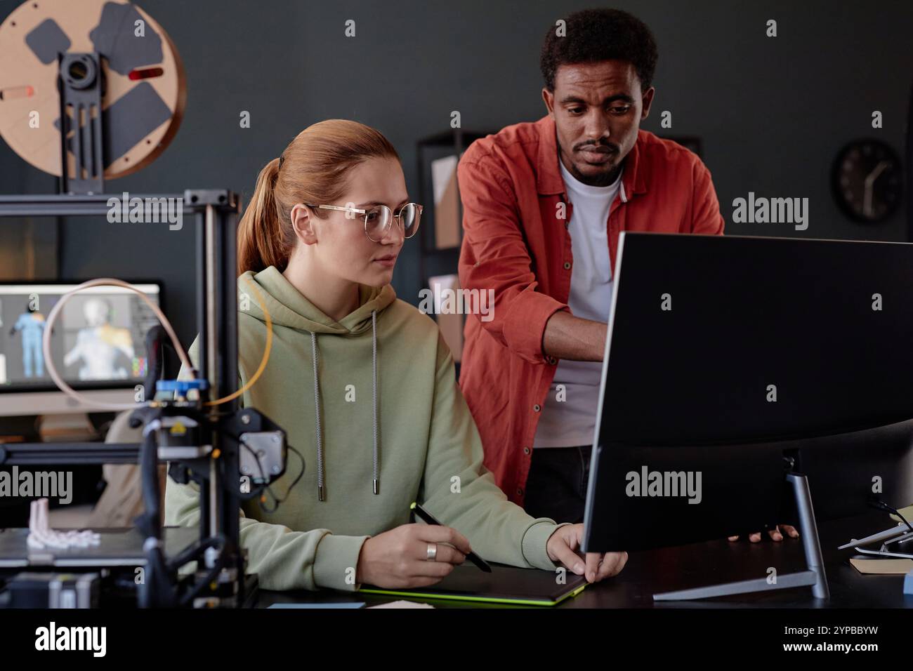 Two colleagues collaborating on project in modern workspace, involving 3D printing and computer ...