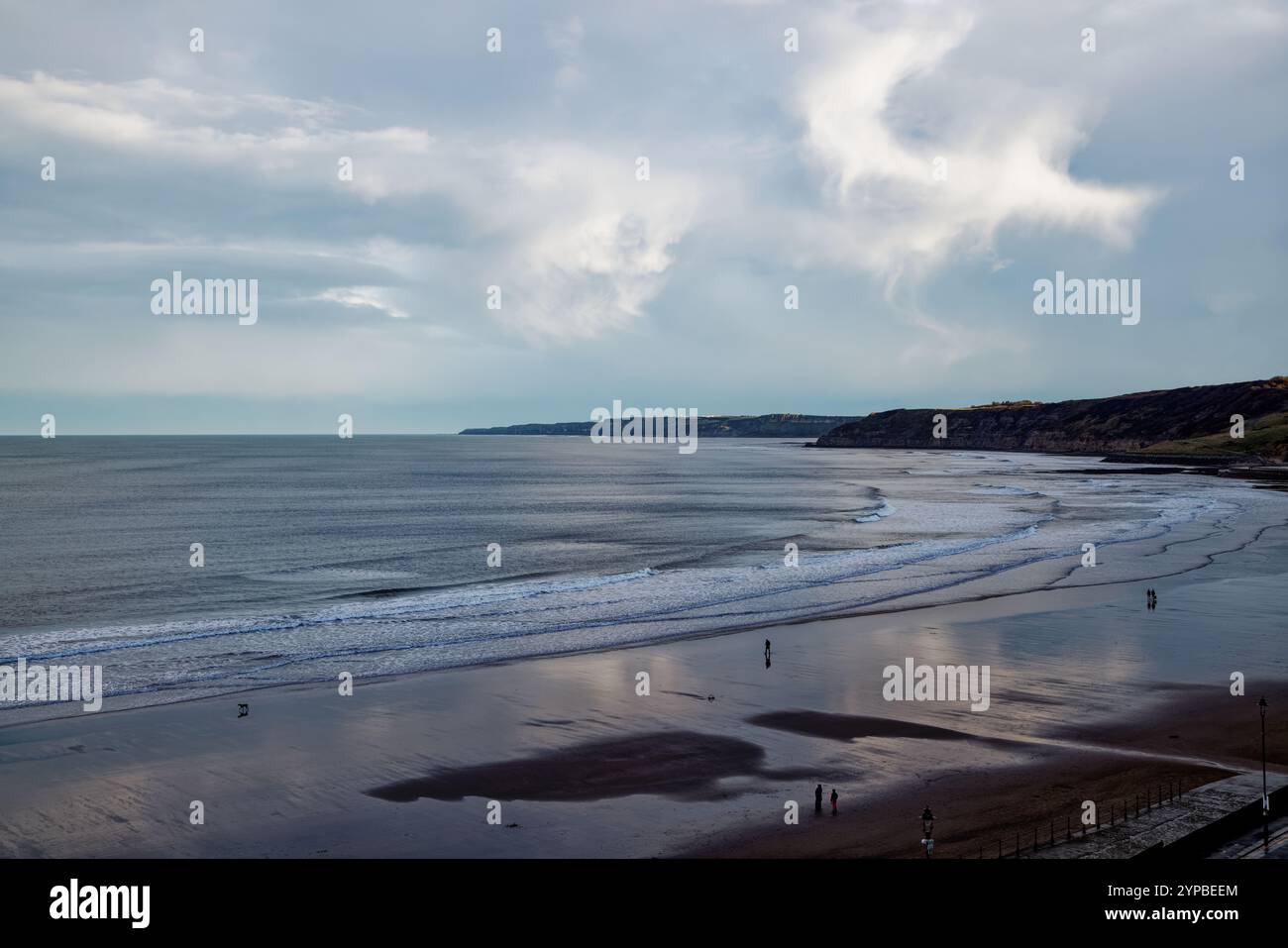 Scattered people walk the wet sand of Scarborough South Bay, England ...