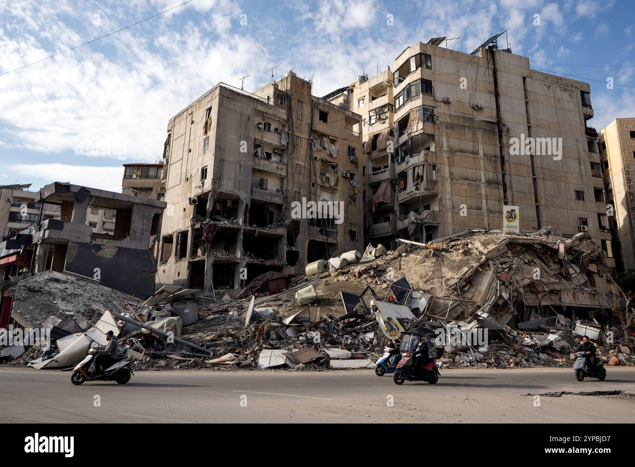 People on their scooter drive past destroyed buildings in Dahiyeh ...
