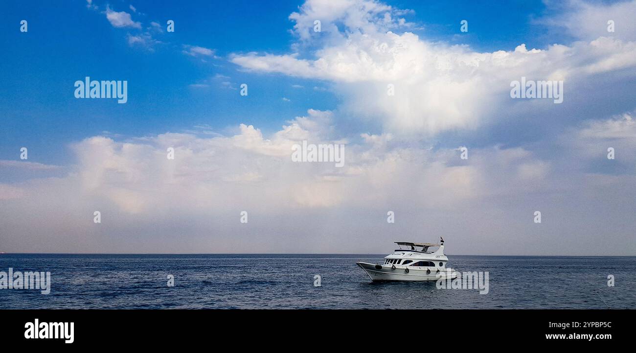 A boat is floating on the ocean. The sky is blue with some clouds. The ...