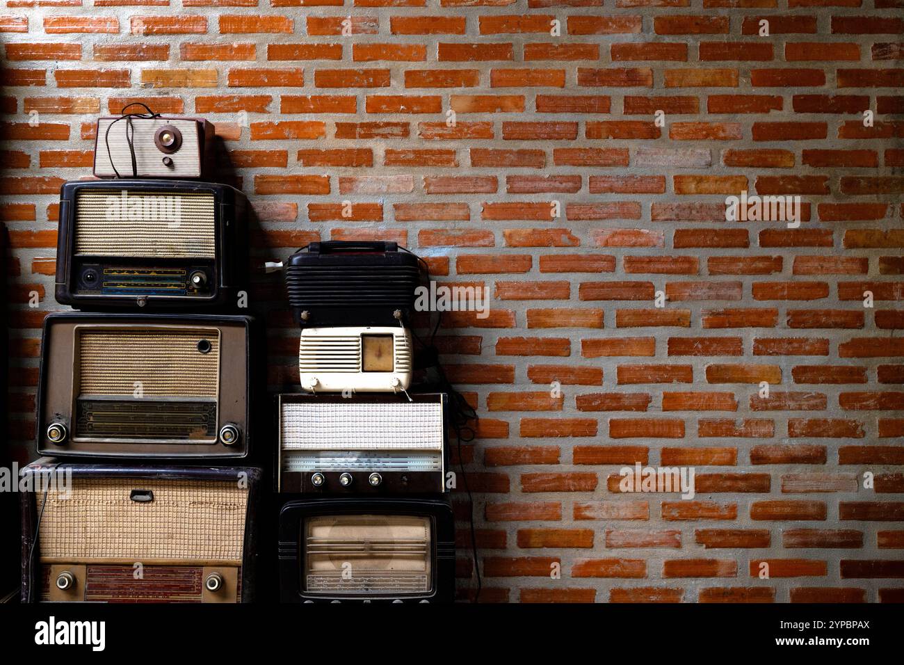 A collection of antique radios stacked against a red brick wall ...