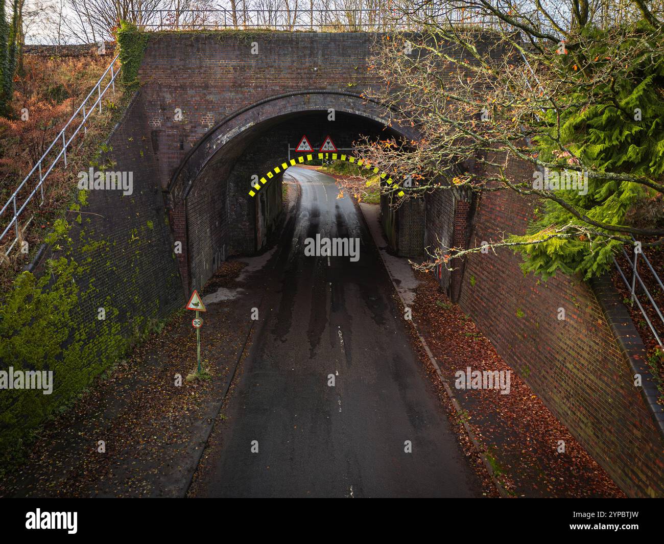 Wet asphalt road with warning signs passing under a low brick bridge in ...