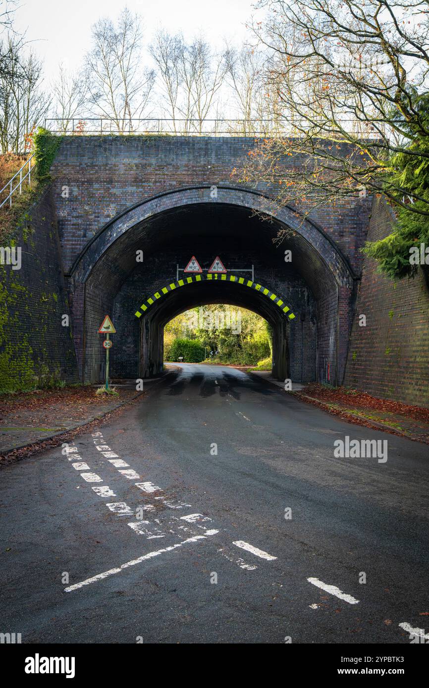 Empty asphalt road passing under an old brick railway bridge with ...