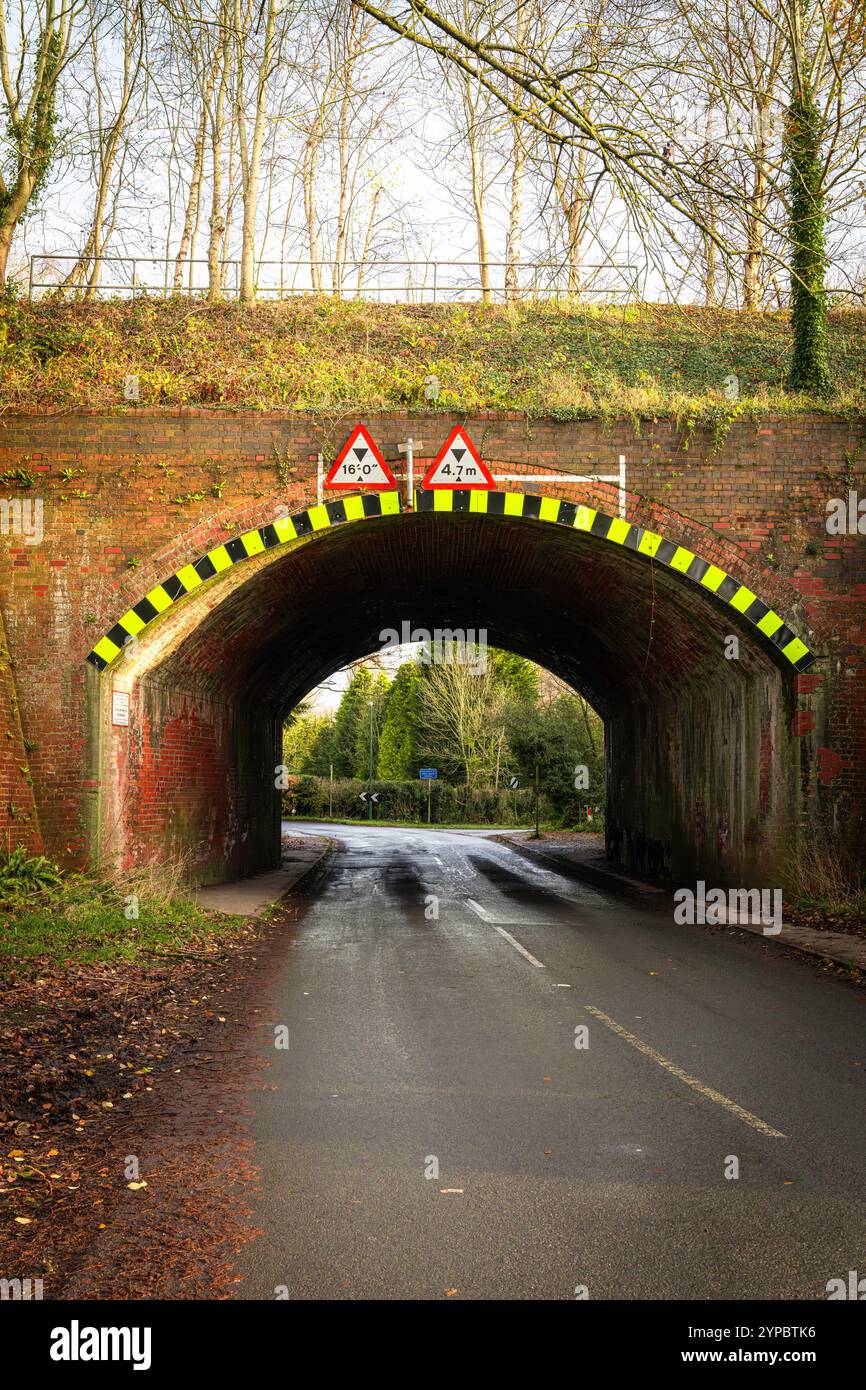 Narrow country road passing under a low railway bridge with height and ...