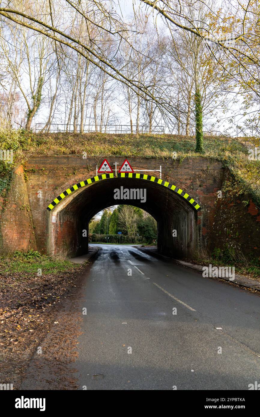 Narrow country lane passing under a low brick railway bridge with ...