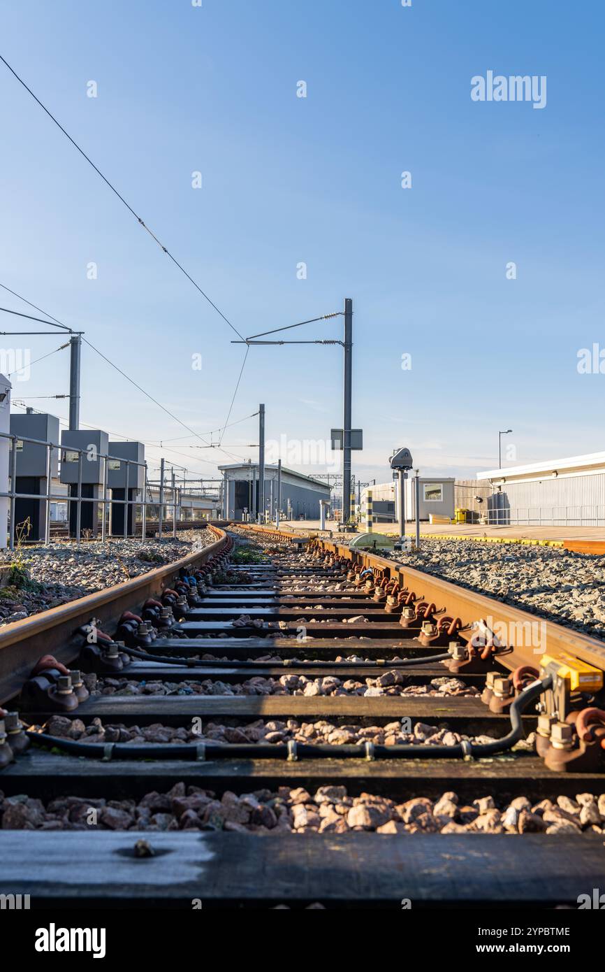 Rusty railway tracks converge towards a vanishing point, stretching into the distance under a ...
