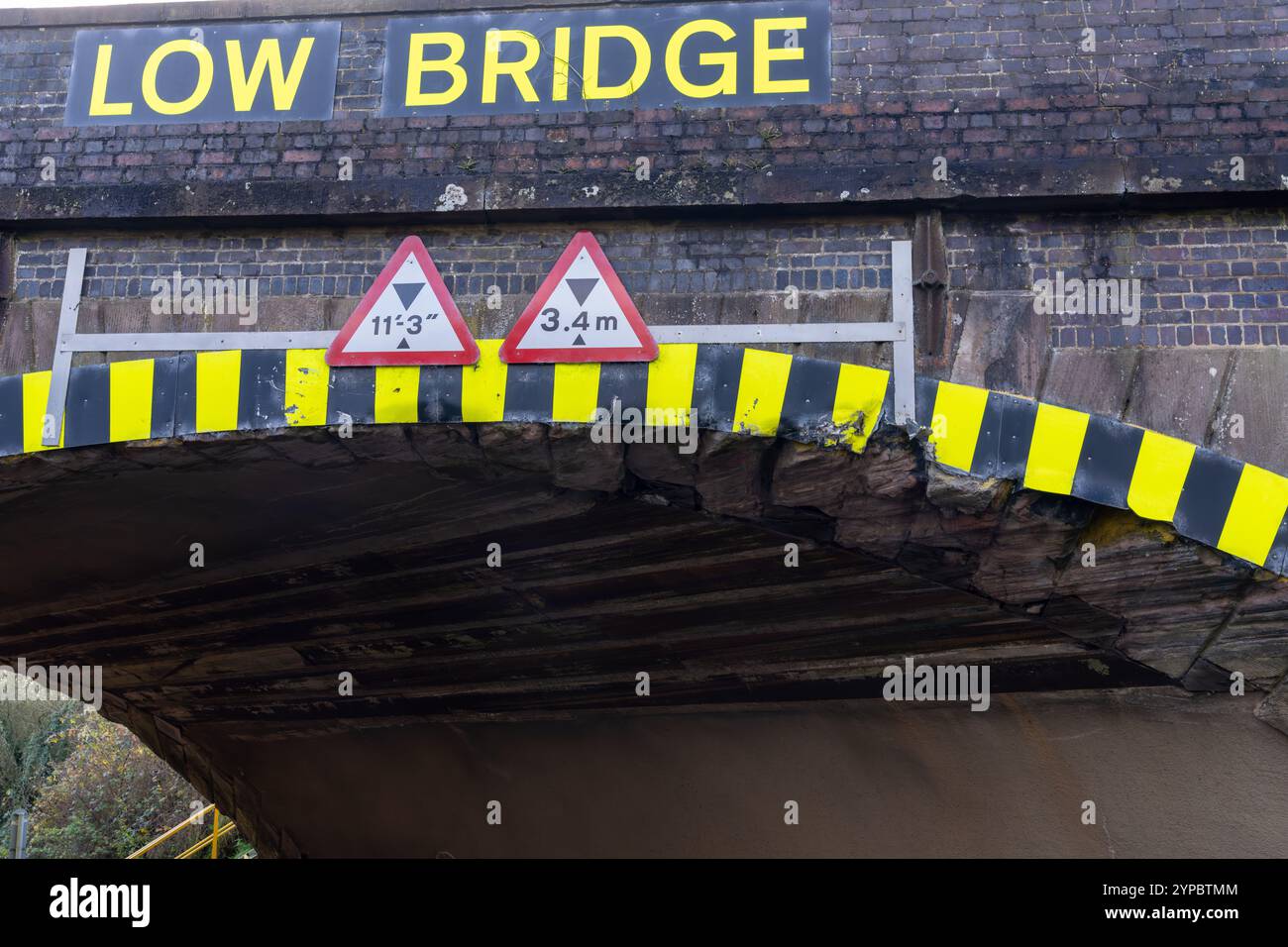 Low bridge sign indicating height restriction with damaged brickwork ...