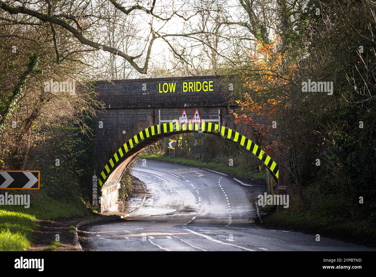 Narrow country road passing under a low bridge with height restriction ...