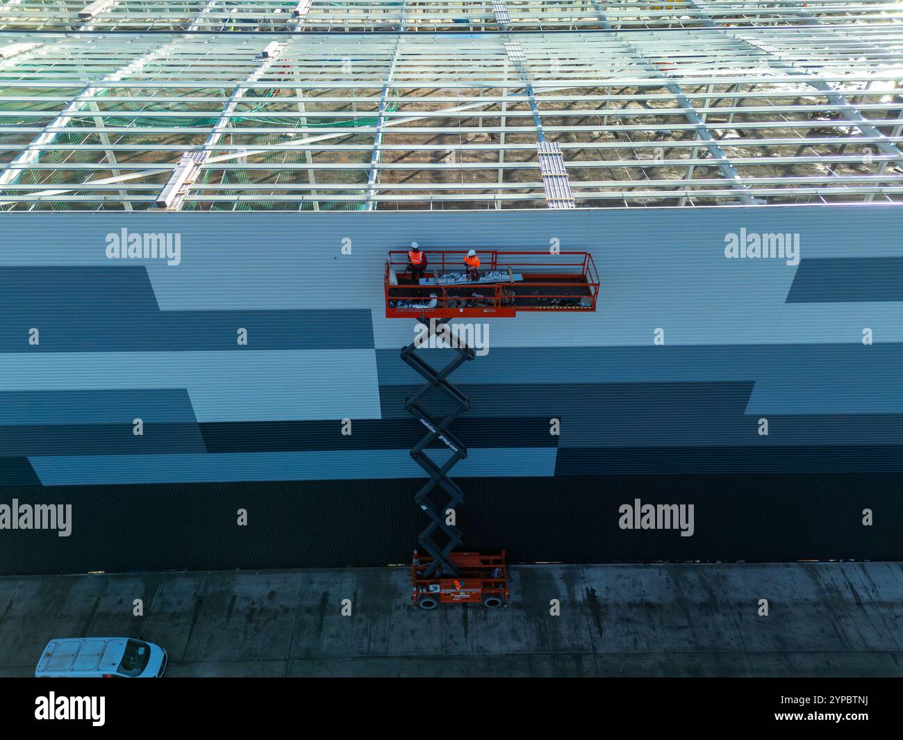 Construction workers using a scissor lift are installing panels on a ...