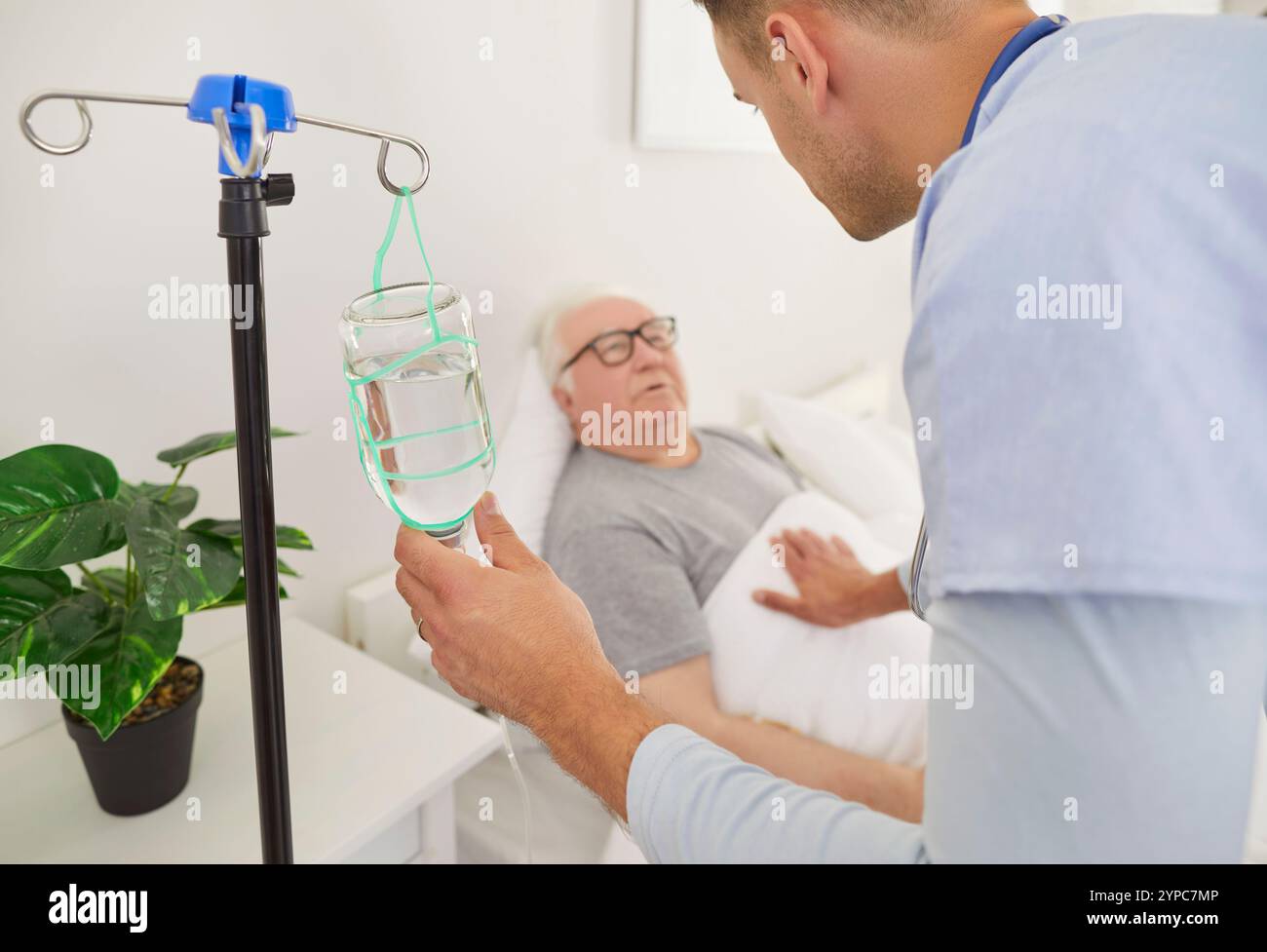 Caring young male nurse checking on elderly patient during IV infusion ...