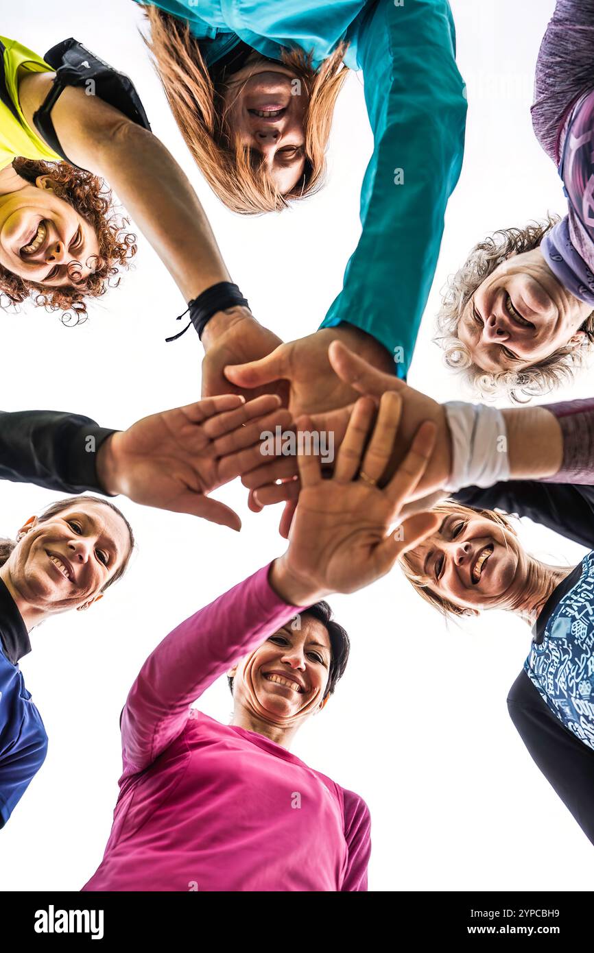 Group of women joining hands in a circle and smiling at the camera. A symbol of teamwork, unity ...